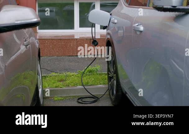 Electric vehicle charging cable connects to a parked car in a ...