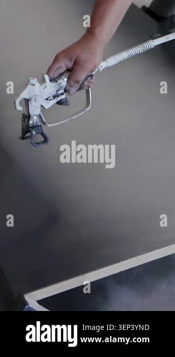Worker is applying paint to wooden board using spray gun while standing ...