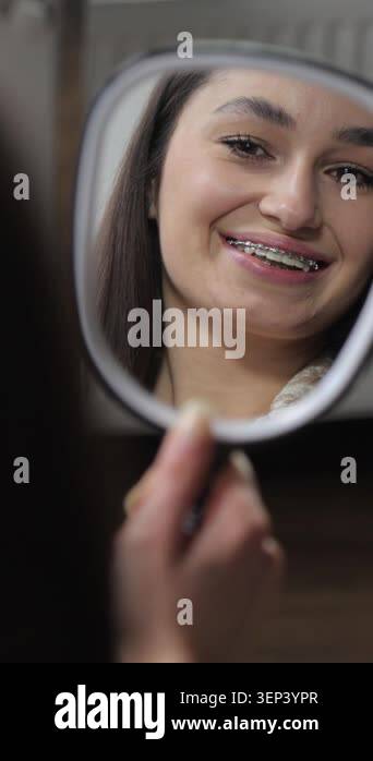 Happy young woman with dental braces holding a mirror and admiring her ...