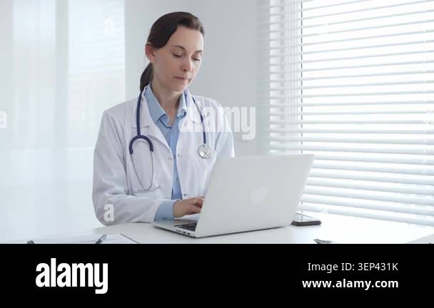Confident female doctor wearing a lab coat and stethoscope sits at a ...