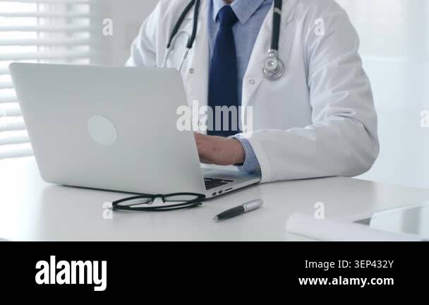 Medical doctor wearing lab coat and stethoscope is sitting at desk and ...