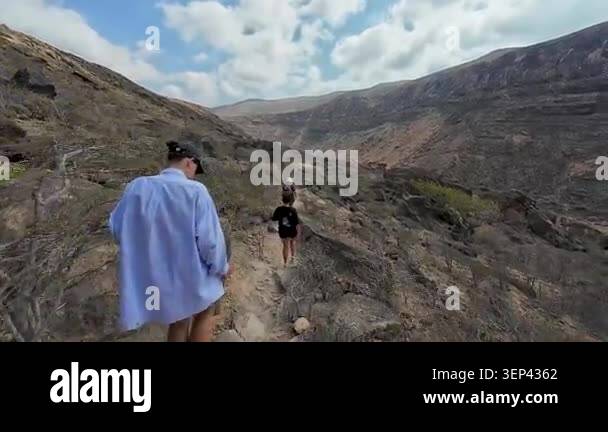 Hikers walking along a narrow rocky mountain trail in a wide canyon ...
