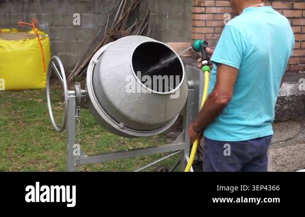 A male builder using a garden hose to spray water inside a rotating ...