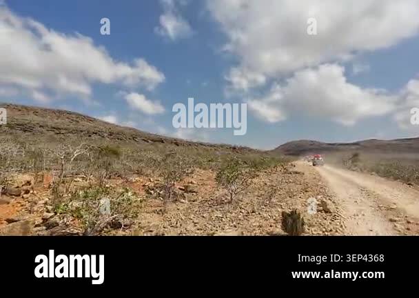 Dusty dirt road crossing a dry hillside under a blue sky with white ...