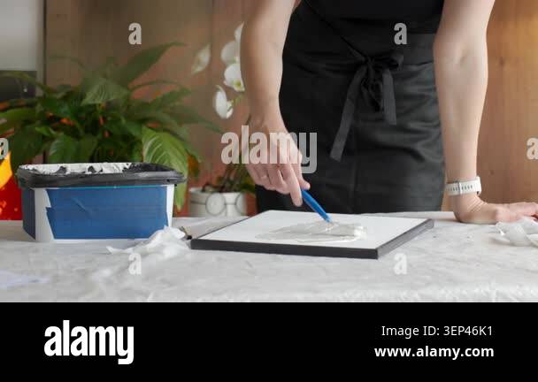 Woman spreads white plaster paste on canvas with a palette knife at a ...