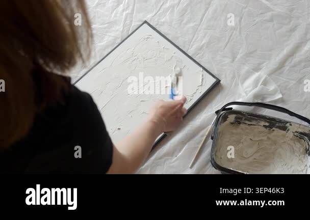 Woman creates a textured picture on canvas, applying white plaster ...