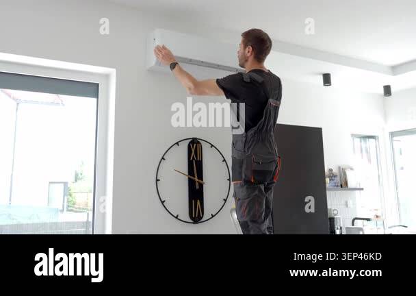 Man checking a wall air conditioner while standing on a ladder in a ...