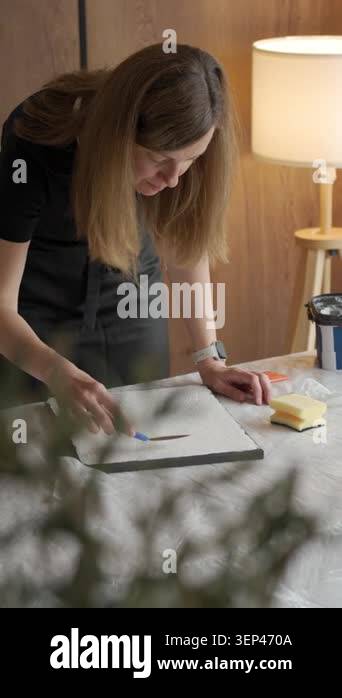 Woman creates textured wall art on canvas, shaping white plaster paste ...
