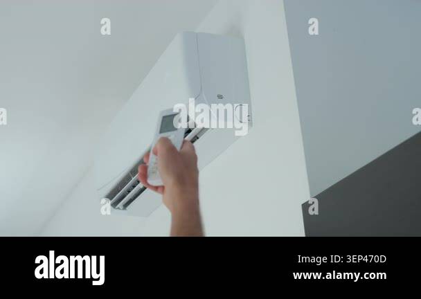 Person uses remote control to adjust a white wall air conditioner in a ...
