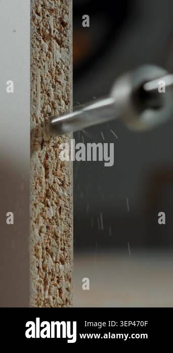 Closeup of a metal drill bit boring into the edge of a particle board ...