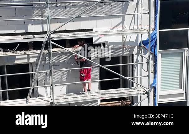 Construction worker sealing window frame on scaffolding with sealant ...