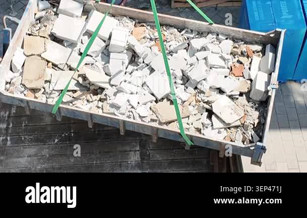 Construction debris being lifted by crane in a skip container at a site ...