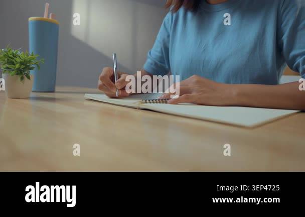 Close-up image of a woman's hand holding a pen and writing on a surface ...