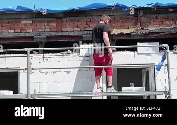 Construction worker on scaffolding installing blocks on building facade ...