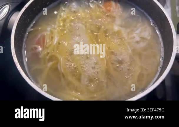 Close up view of spaghetti and cherry tomatoes boiling in hot water ...