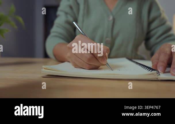 Close-up image of a woman's hand holding a pen and writing on a surface ...