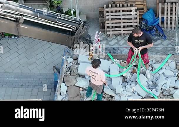 Construction workers use crane to lift heavy debris into a dumpster ...
