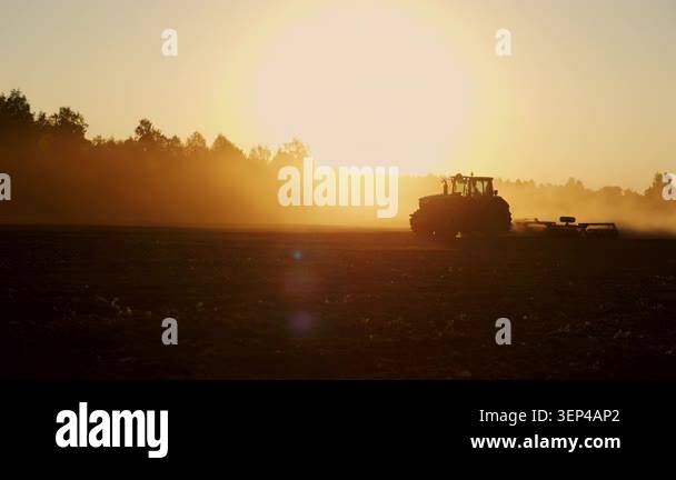 Silhouette of agricultural tractor cultivating farmland at sunset ...