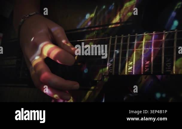 Close-up of a female hand playing electric guitar, illuminated by ...