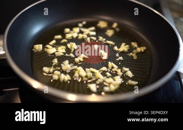 Chopped garlic pieces frying in olive oil inside a black non-stick pan ...