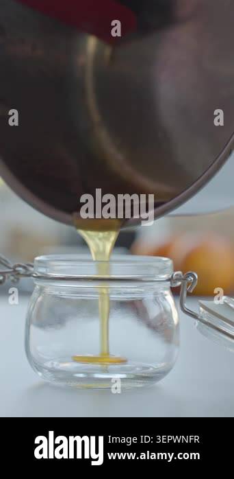 Golden orange syrup pours from saucepan into glass jar. Concept of ...