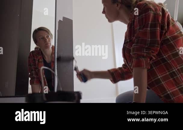 Woman paints dark door frame with small roller beside mirror reflection ...