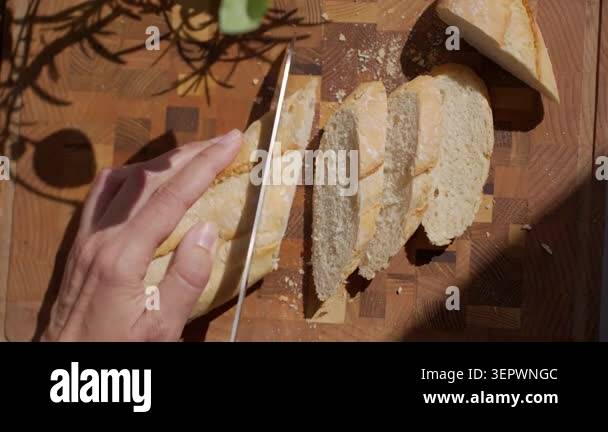 Person cuts baguette into slices with knife on cutting board in ...