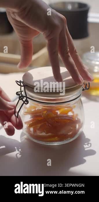 Hand opens glass jar and takes candied orange peel. Concept of homemade ...