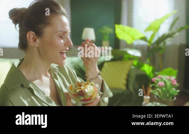 A happy woman enjoys a nutritious snack of mixed fruit salad in her ...