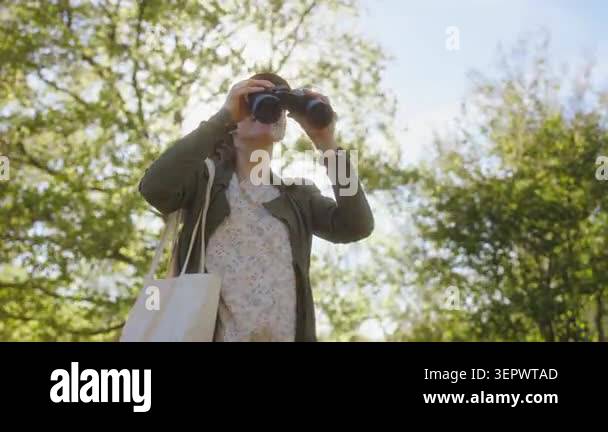 A woman in a cap and green jacket laughs while using binoculars to ...