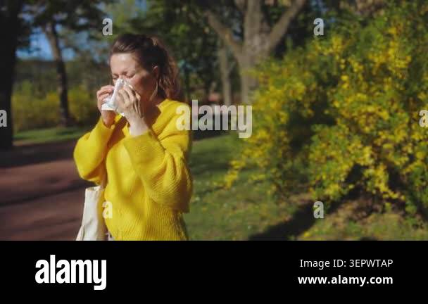 A woman in a yellow sweater deals with hay fever symptoms, blowing her ...
