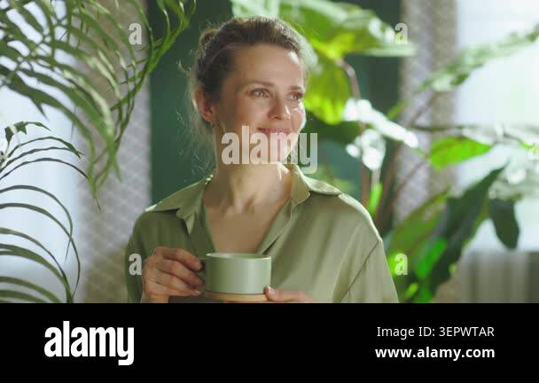A happy woman sips from a green ceramic mug, enjoying a quiet moment of ...