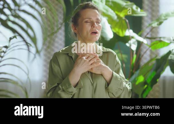 Close-up of a calm woman in a green shirt with her hands on her chest ...