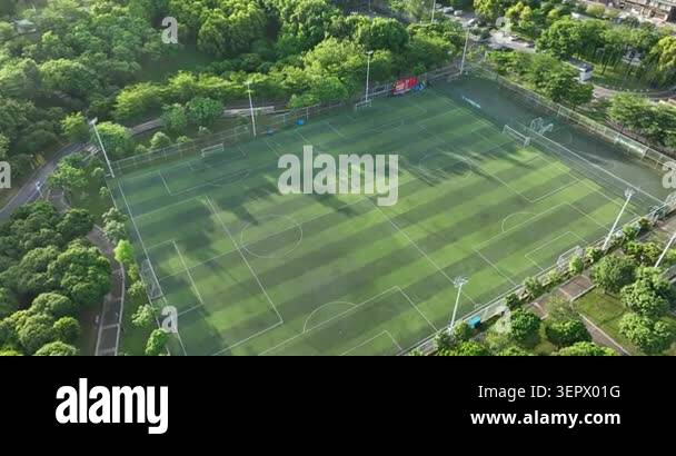 Aerial drone footage of an empty soccer field surrounded by lush green ...