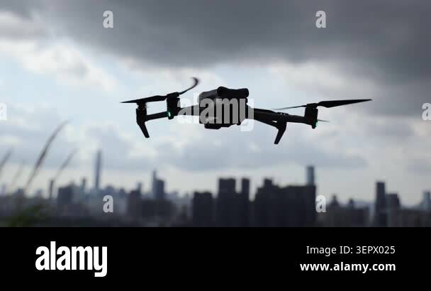 Silhouette of a drone flying in the sky with a city skyline in the ...