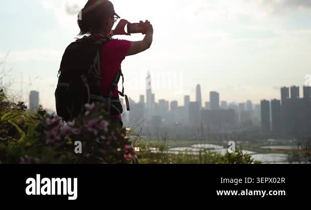 A woman with a backpack takes a photo of a cityscape with her ...