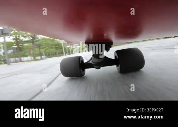 Low angle view from beneath a red skateboard as it moves along a paved ...