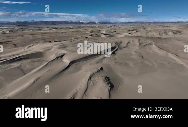 Aerial drone footage flying over vast sand dunes with distant mountains ...