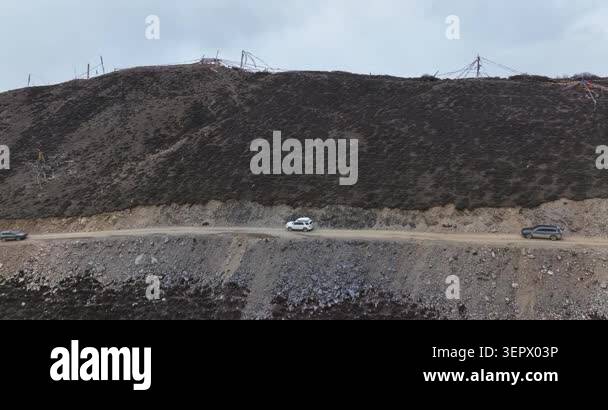 Aerial view of cars driving on a dirt road along a barren mountainside ...