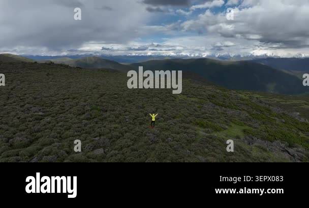 Aerial drone footage of a person standing on a vast, green, mountainous ...