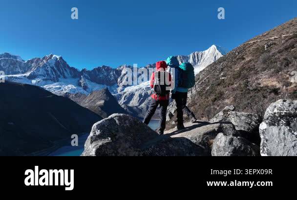 Two hikers with backpacks stand on a rocky outcrop, admiring a vast ...