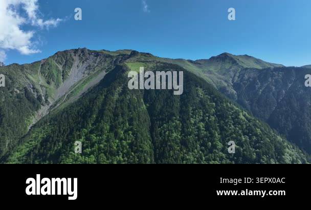 Aerial drone footage flying over a lush green mountain covered in dense ...