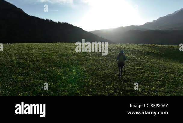 A lone hiker with a backpack walks across a grassy field towards ...