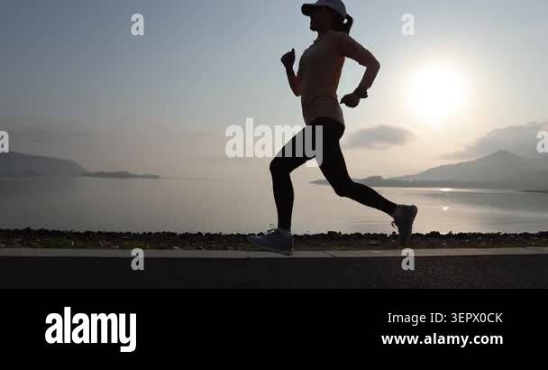 Silhouette of a woman running along a waterfront at sunrise, with ...