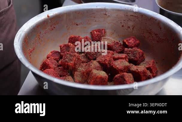 Close-up of cubed meat being seasoned with spices in a metal bowl ...