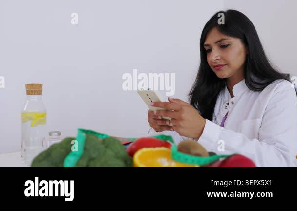 Female dietitian in a white coat working on a mobile phone, with fresh ...
