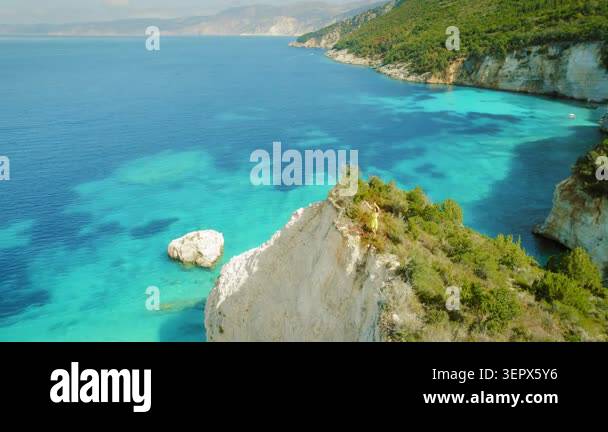 Woman dancing on cliff with vibrant blue water and dramatic rocky ...