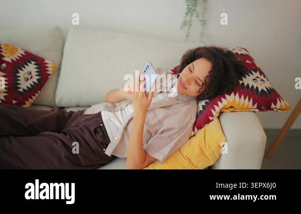 Young African American woman with curly hair lying on a sofa at home ...