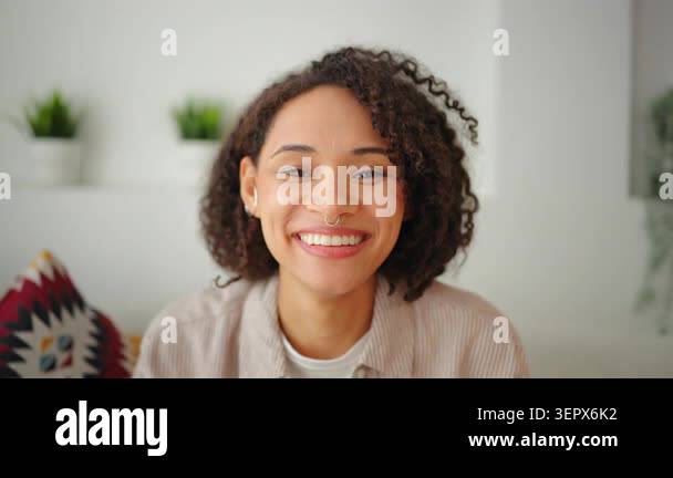 Young African American woman with curly hair sitting on a sofa, smiling ...