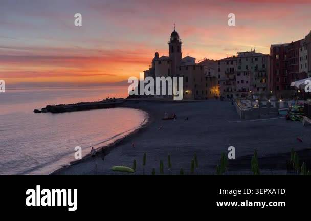 People stroll along the beach in Camogli, Italy. The sun sets in the ...